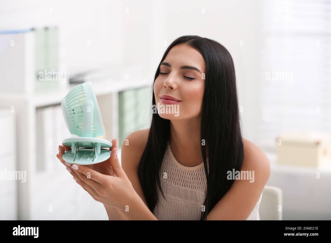 Young woman enjoying air flow from fan at workplace Stock Photo - Alamy