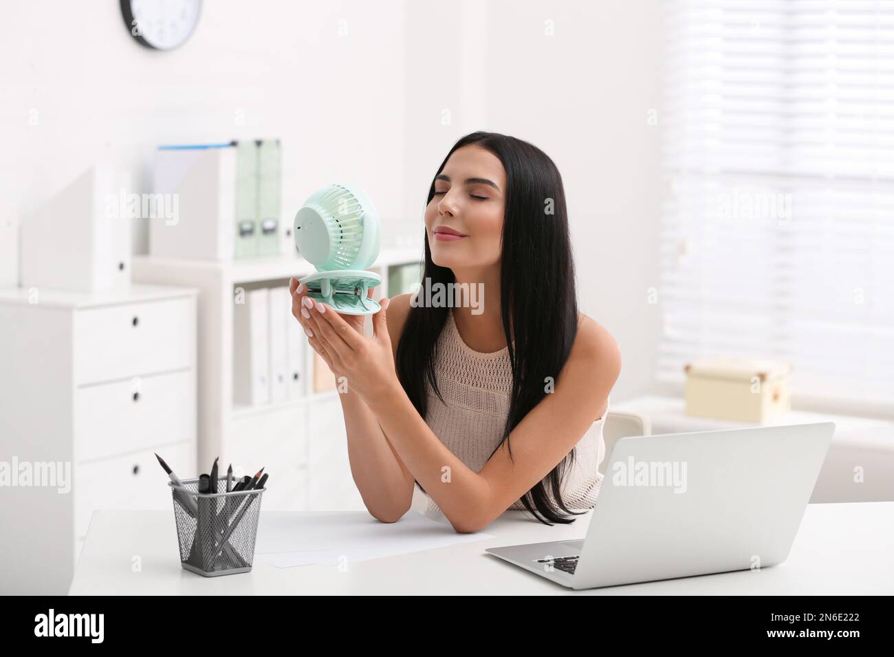 Young woman enjoying air flow from fan at workplace Stock Photo - Alamy