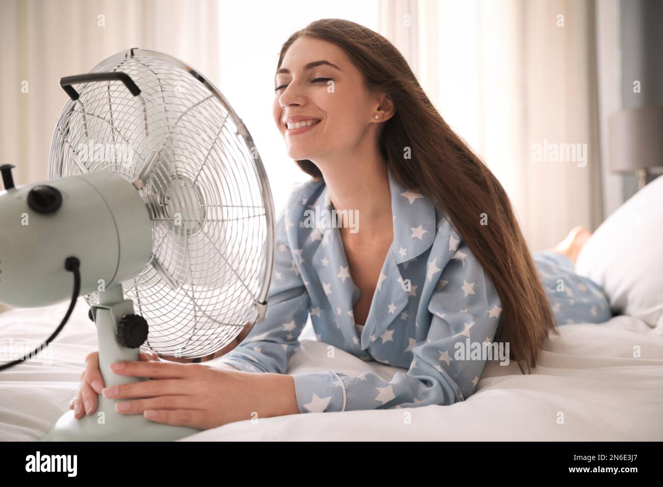 Woman enjoying air flow from fan on bed in room. Summer heat Stock ...