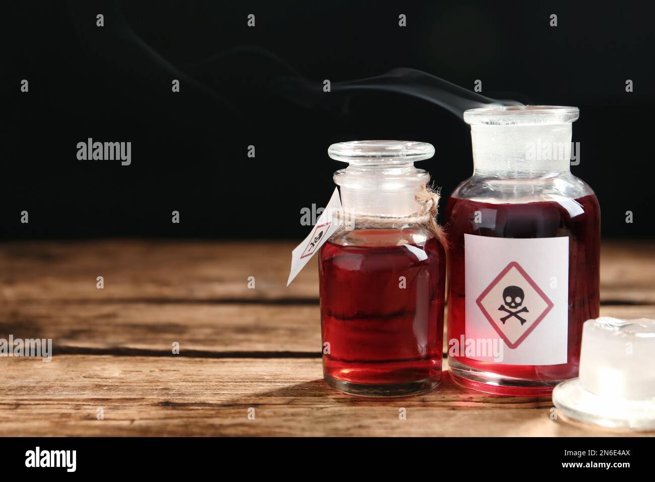Glass bottles of poison with warning signs on wooden table. Space for ...