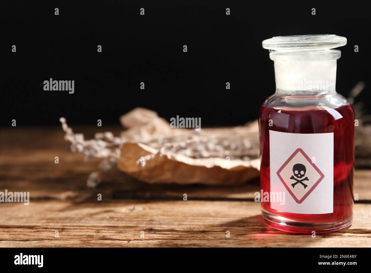 Glass bottle of poison with warning sign on wooden table. Space for ...