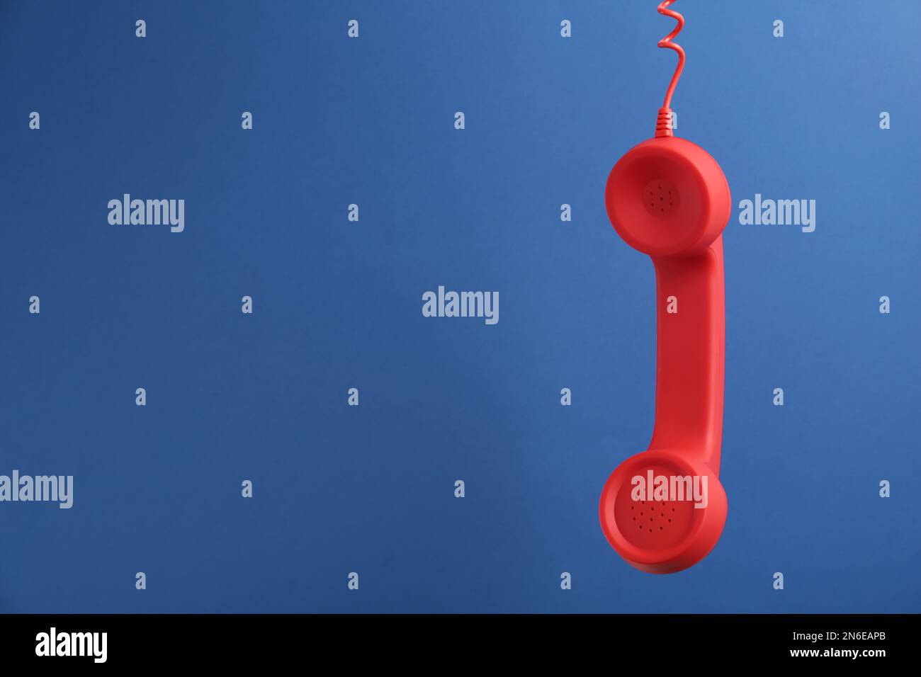 Red corded telephone handset hanging on blue background, space for text ...