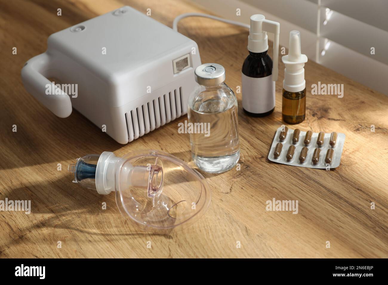 Modern nebulizer with face mask and medications on wooden table indoors ...