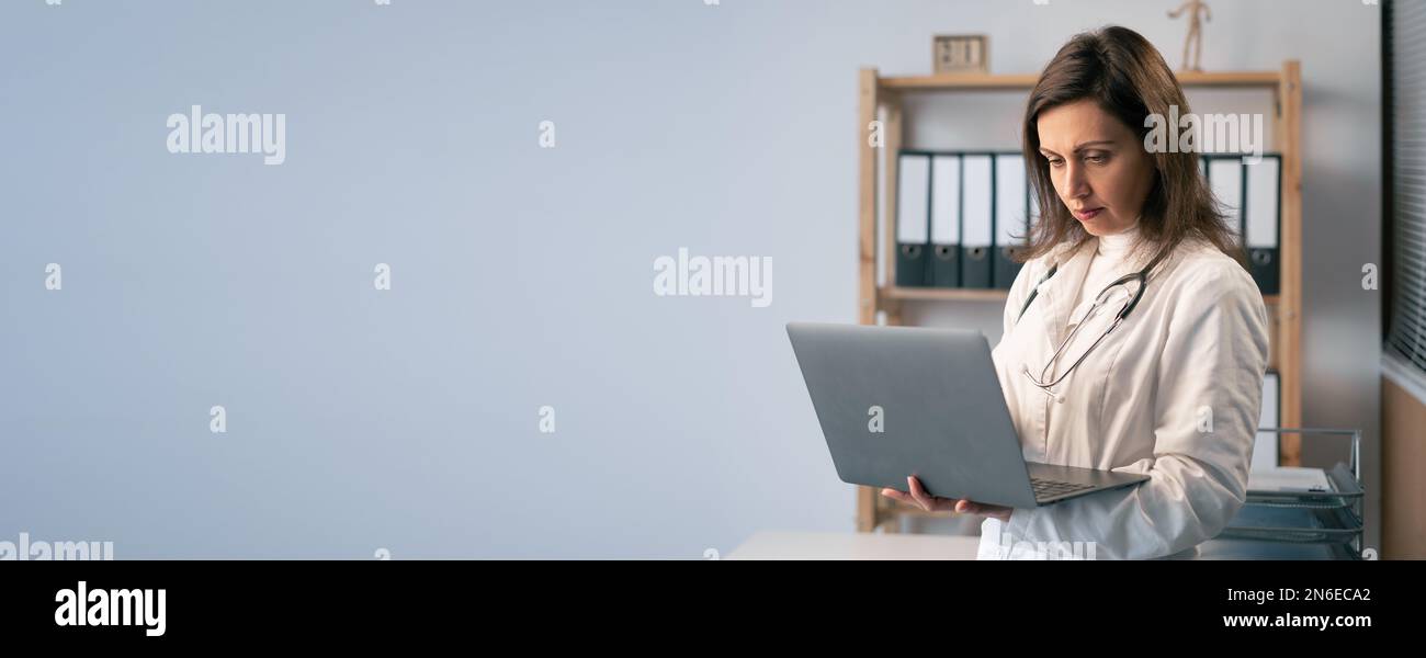 Doctor working with laptop computer while standing in medical workspace ...