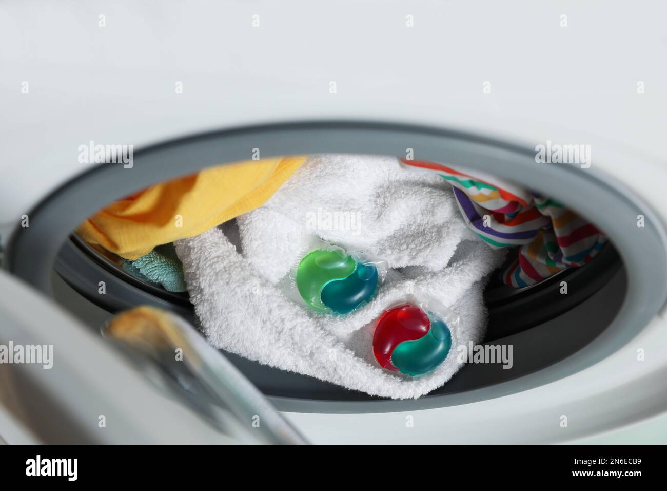 Laundry detergent capsules and clothes in washing machine drum, closeup ...