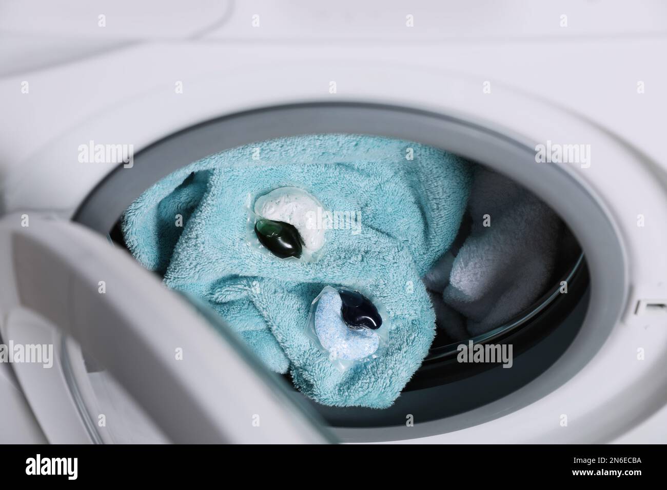 Laundry detergent capsules and towels in washing machine drum, closeup ...