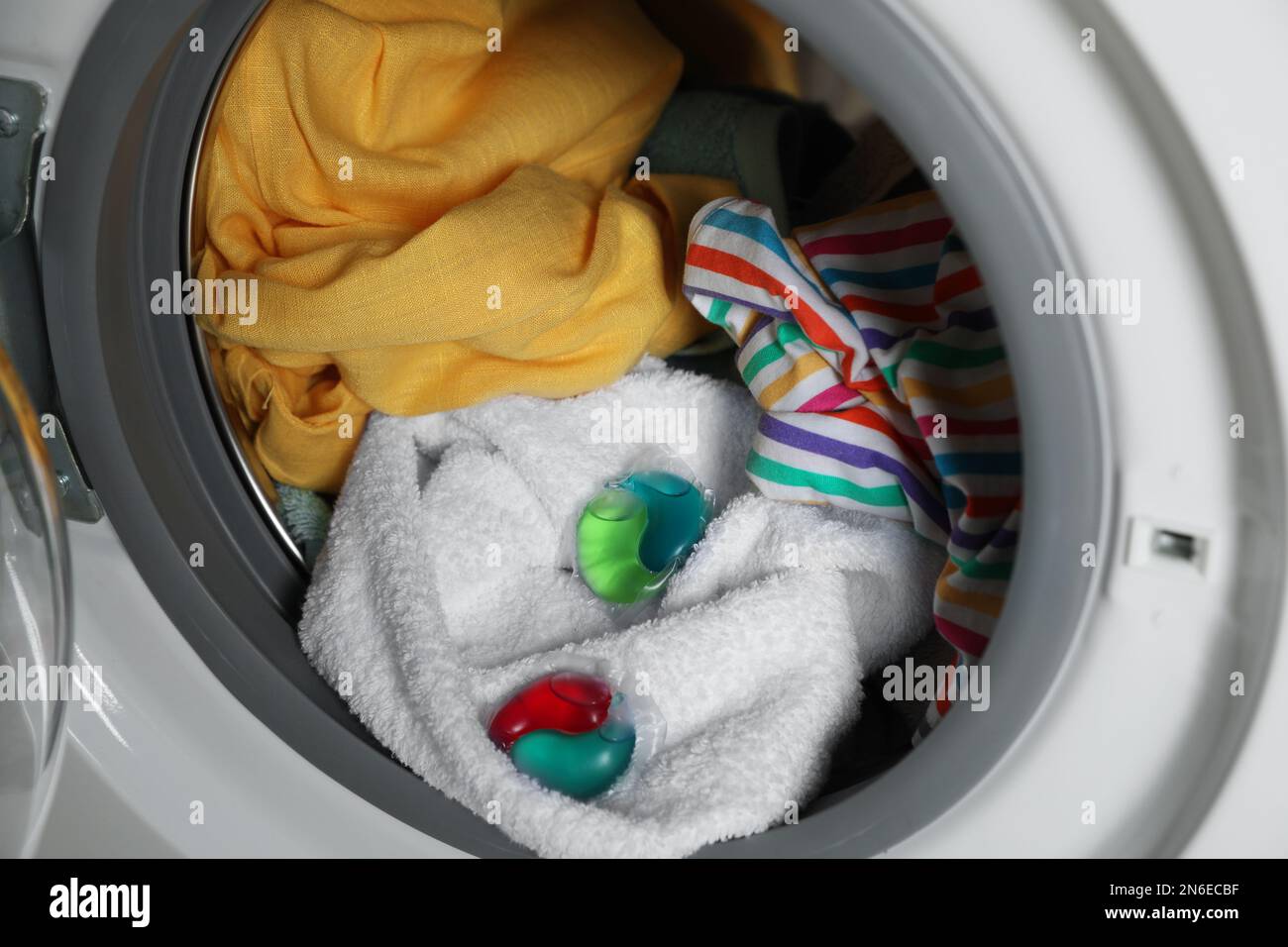Laundry detergent capsules and clothes in washing machine drum, closeup ...