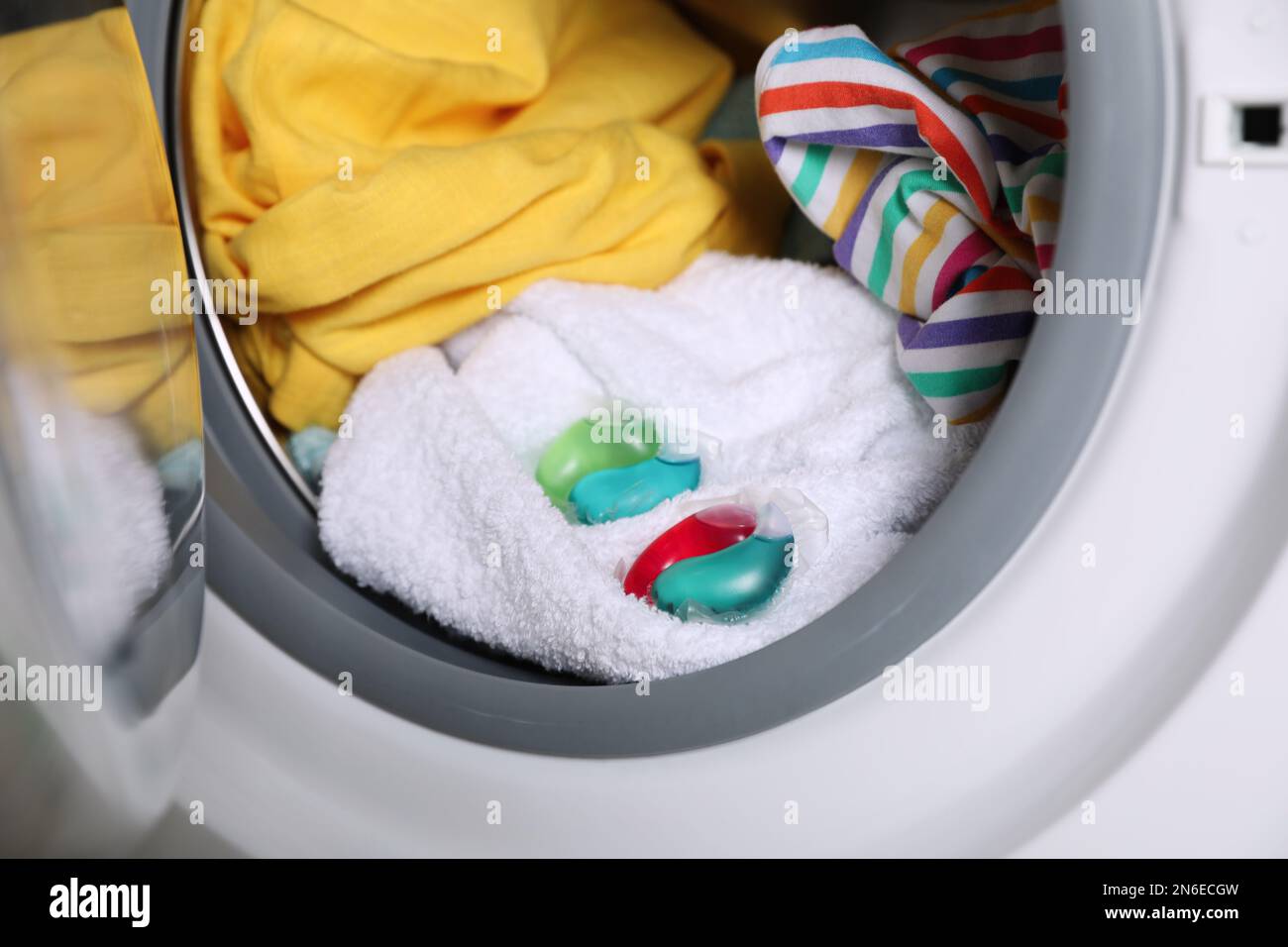 Laundry detergent capsules and clothes in washing machine drum, closeup ...