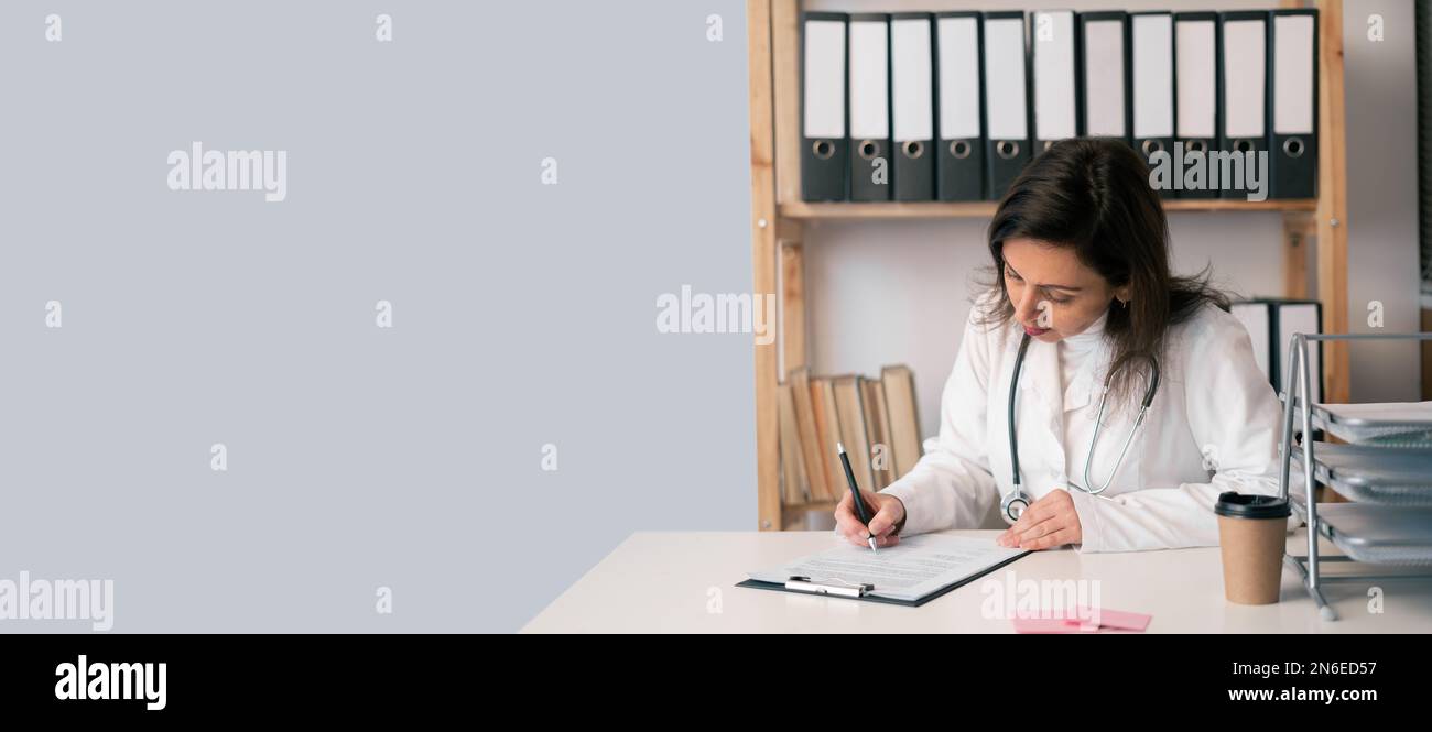 Female doctor writing something on clipboard sitting on workplace in ...