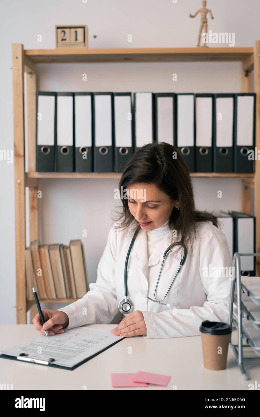 Indian female GP making notes with pen in clipboard while receiving ...