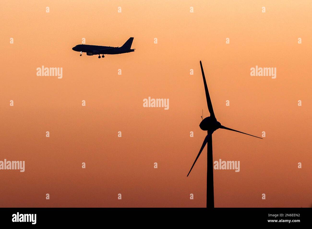 Airplane silhouetted flying past a wind turbine at early dawning Stock ...