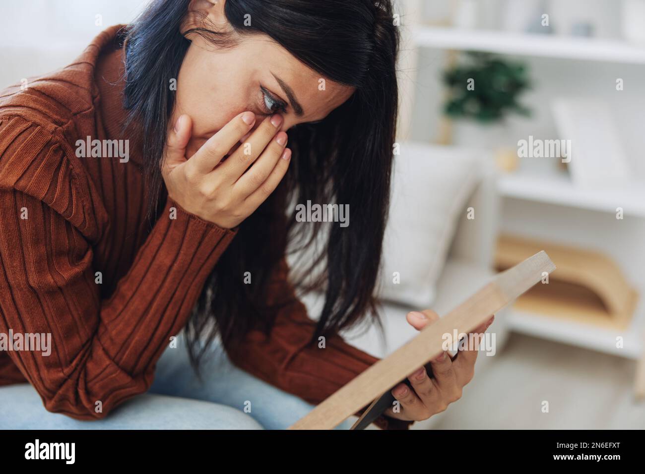 The woman looks sadly at the picture frames in her hands and with ...