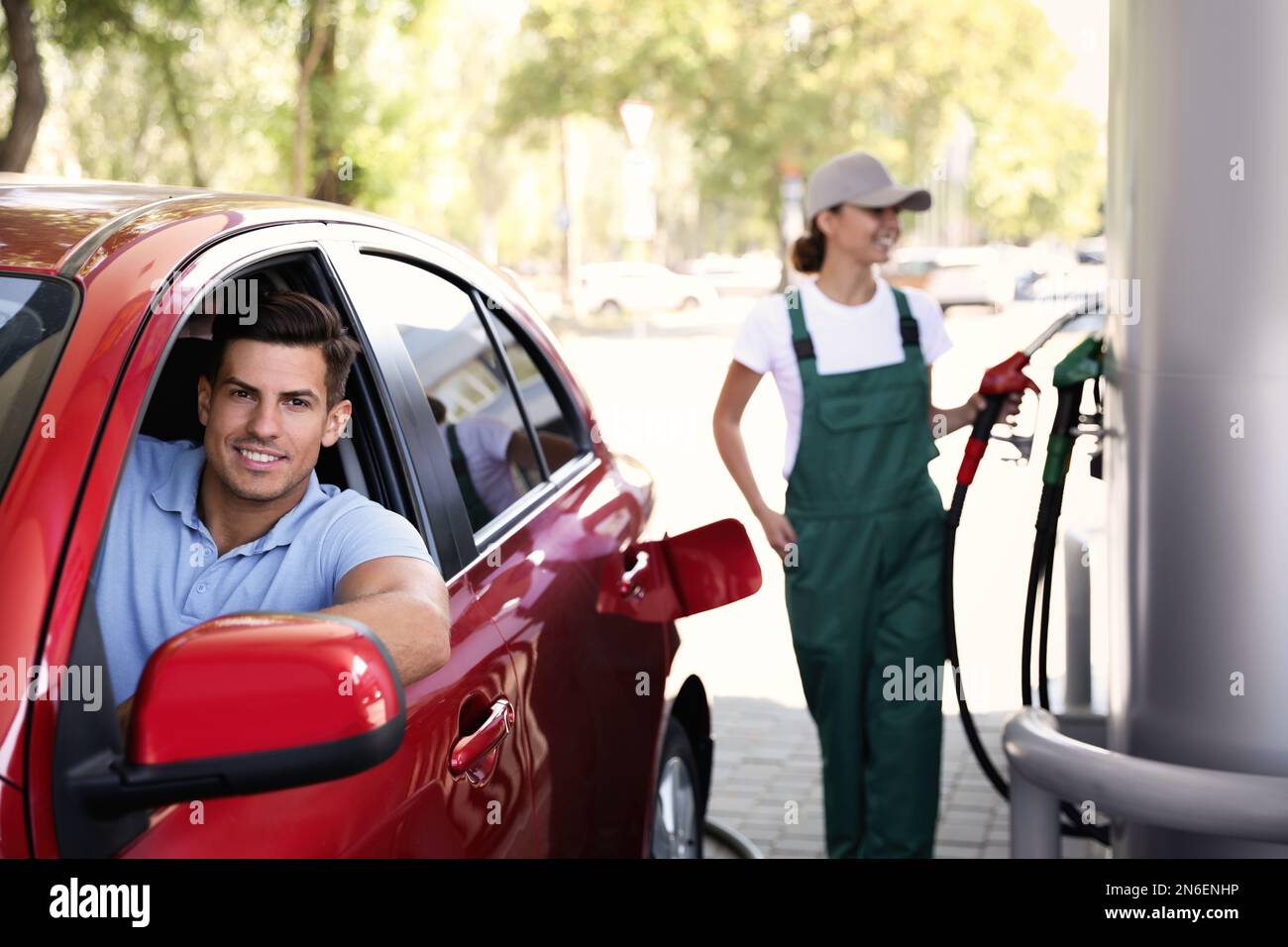 Man sitting in car while young worker refueling his auto at modern gas ...