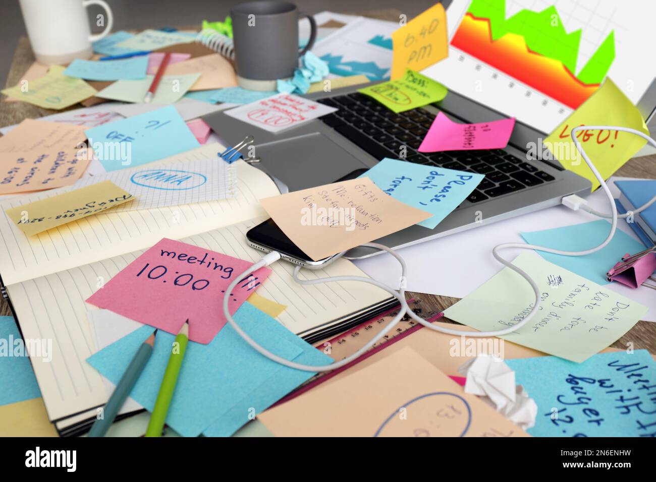 Laptop, notes and office stationery in mess on desk. Overwhelmed with ...