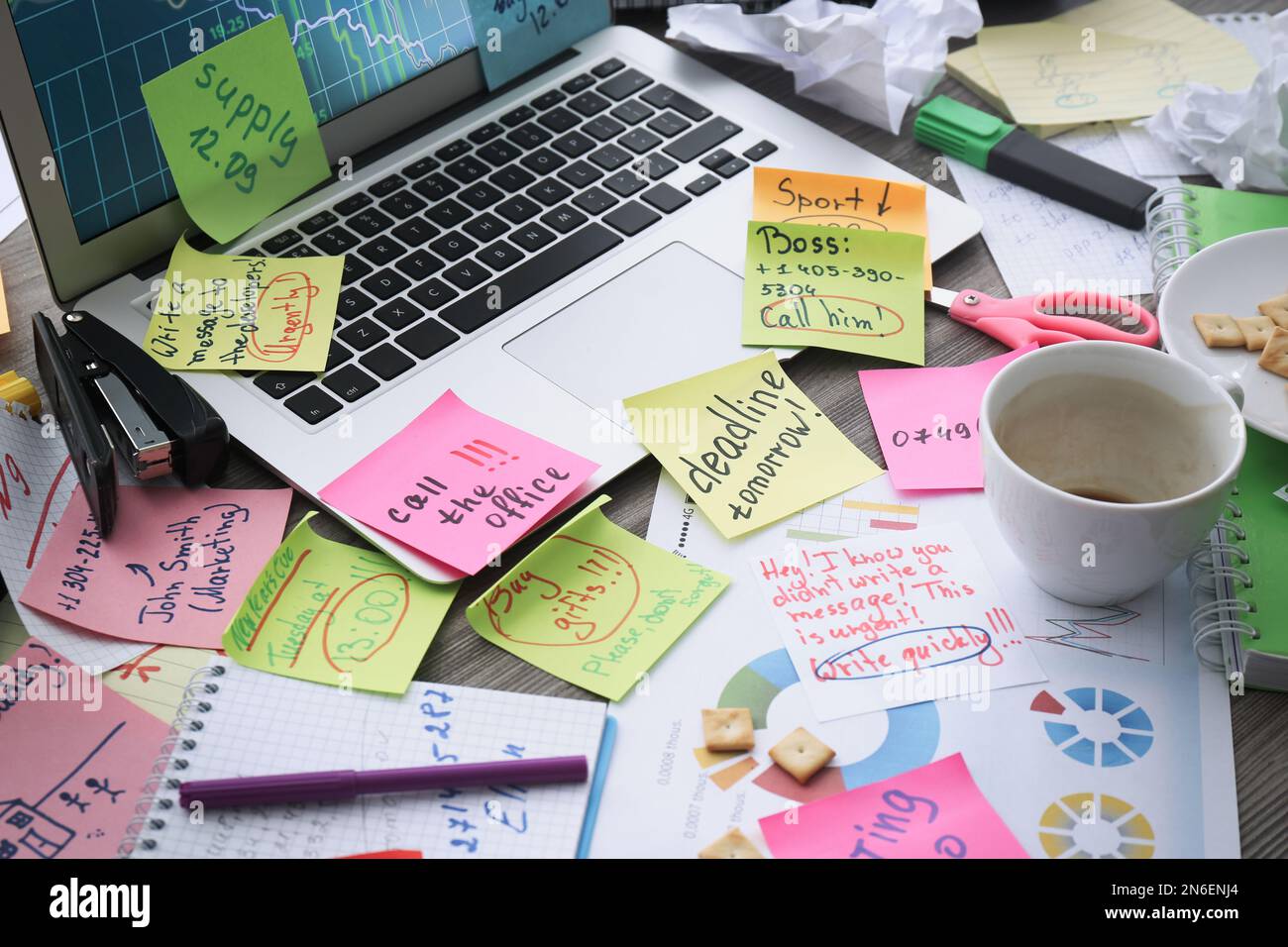 Laptop, notes and office stationery in mess on desk. Overwhelmed with ...