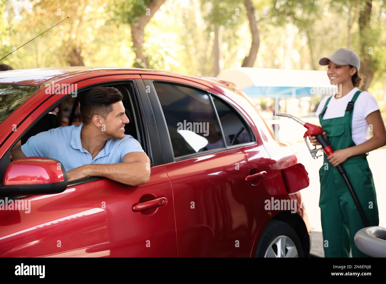 Man sitting in car while young worker refueling his auto at modern gas ...