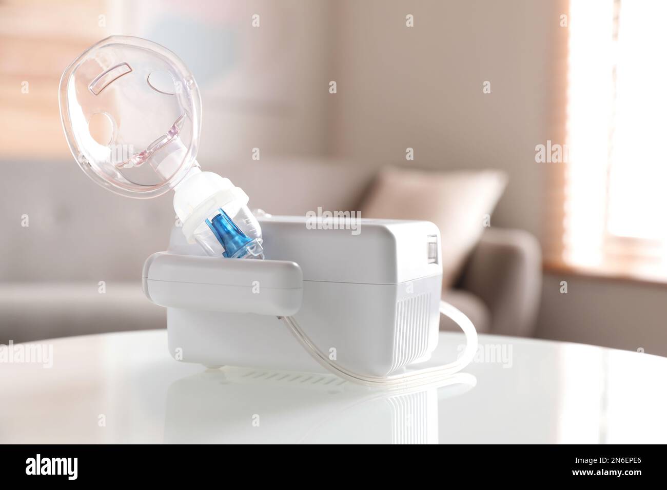Modern nebulizer with face mask on white table indoors. Inhalation ...