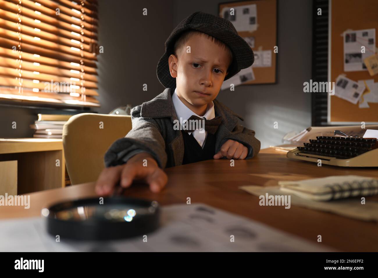Cute little detective taking magnifying glass at table in office Stock ...