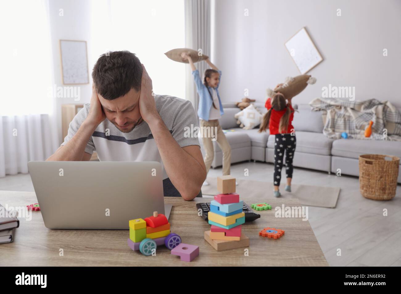 Children disturbing stressed man in living room. Working from home ...