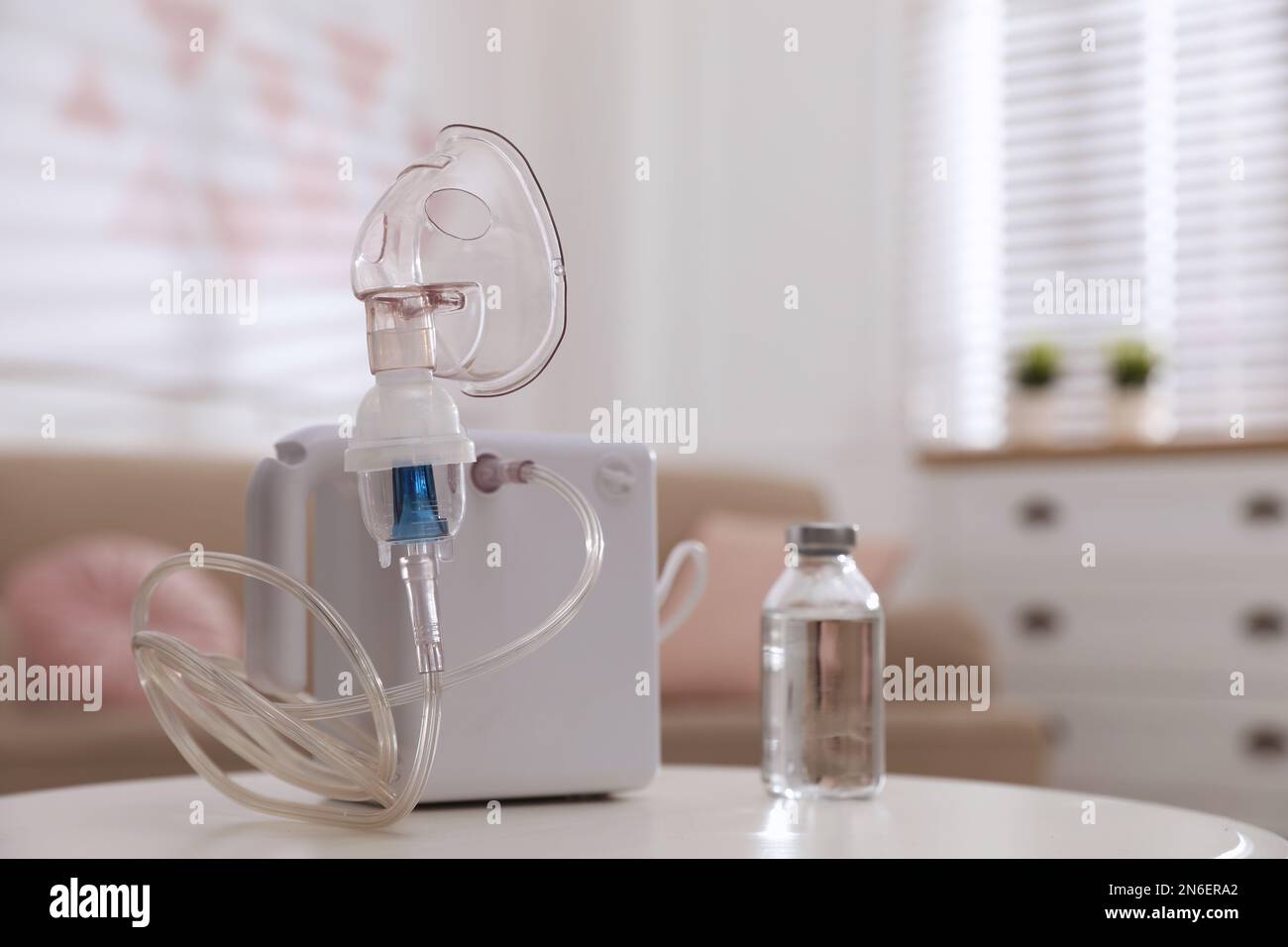 Modern nebulizer with face mask and liquid medicine on white table ...