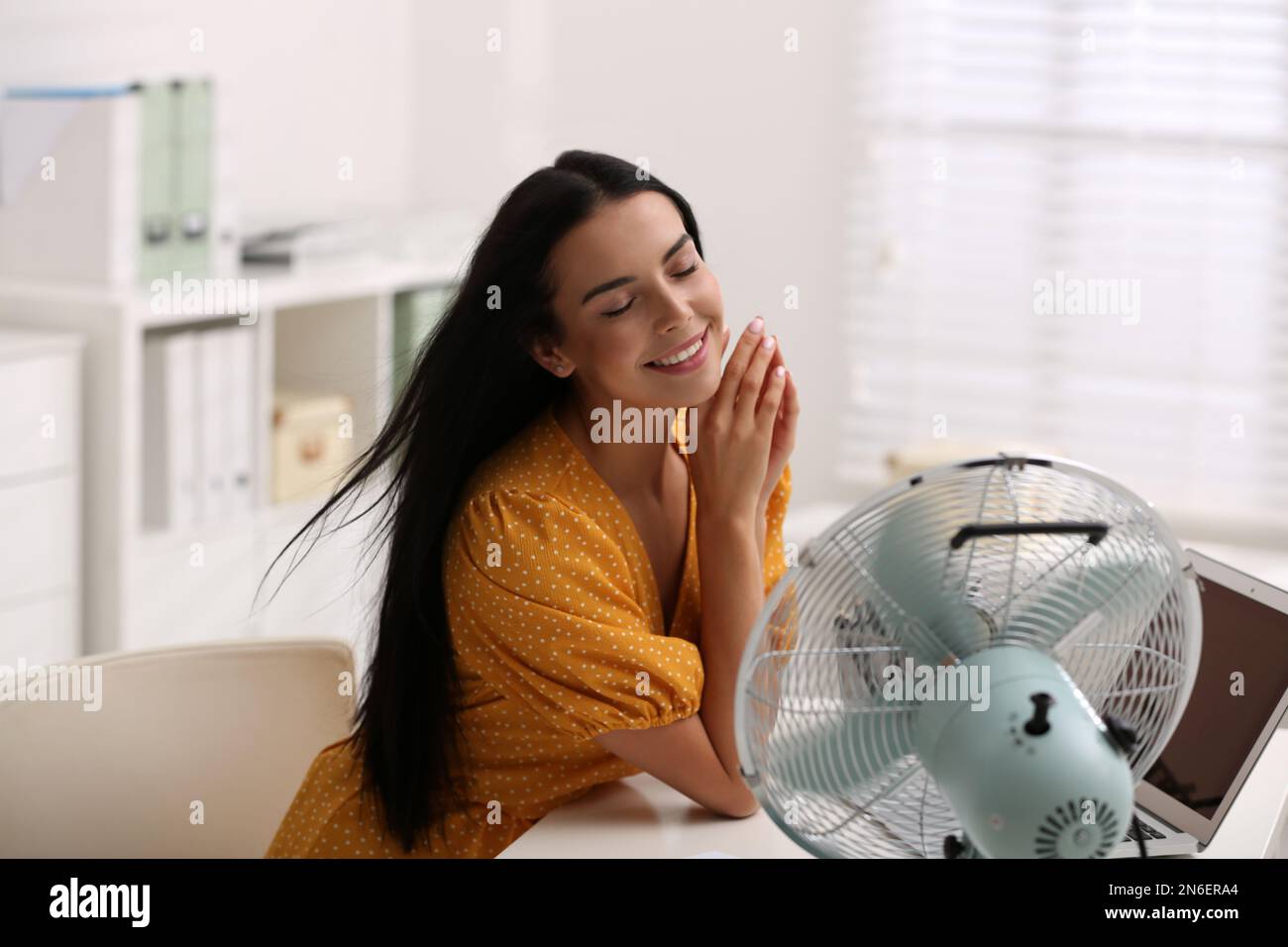 Young woman enjoying air flow from fan at workplace Stock Photo - Alamy
