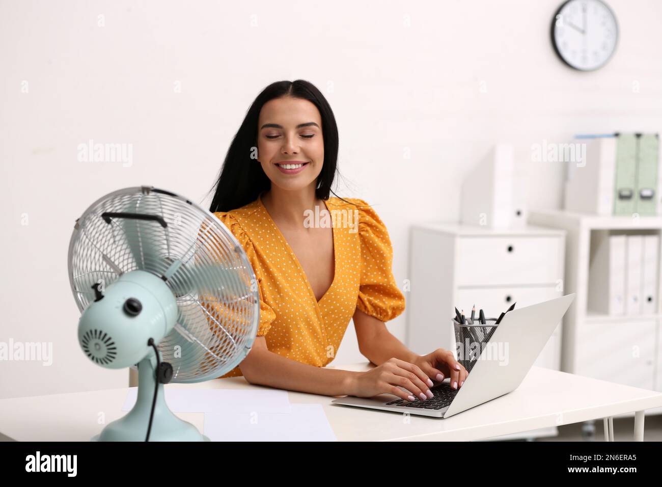 Young woman enjoying air flow from fan at workplace Stock Photo - Alamy