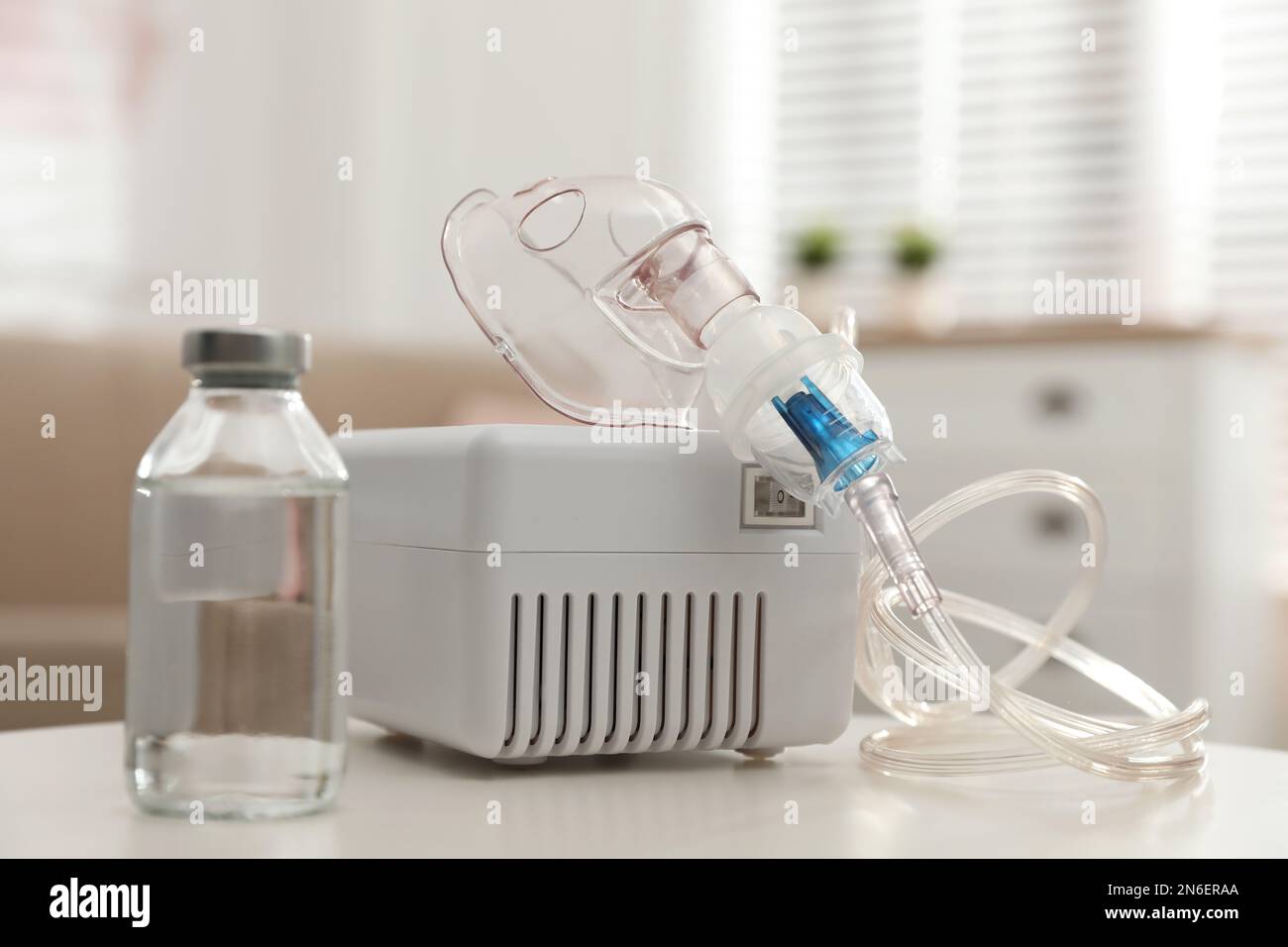 Modern nebulizer with face mask and liquid medicine on white table ...