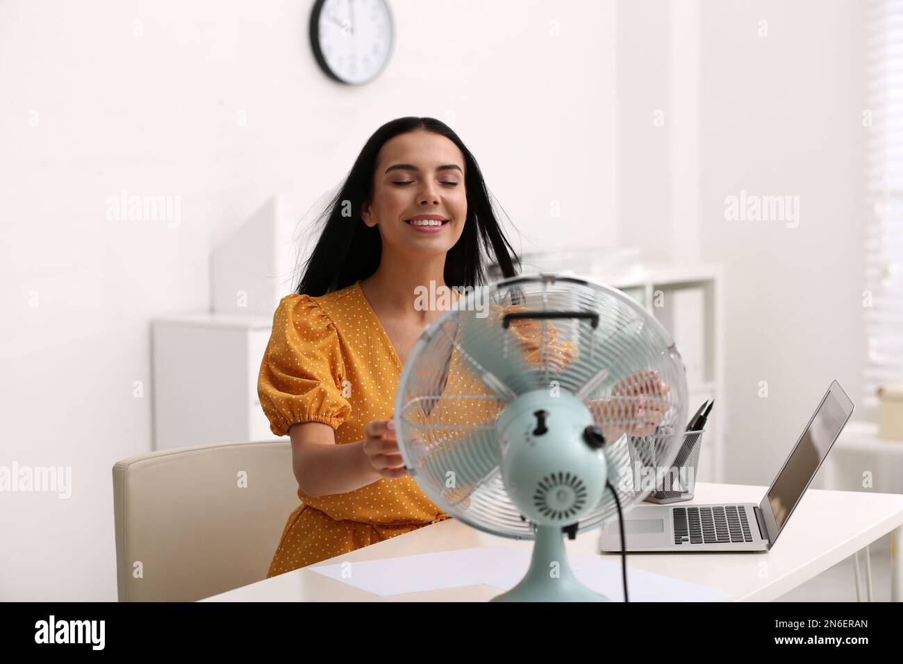 Young woman enjoying air flow from fan at workplace Stock Photo - Alamy