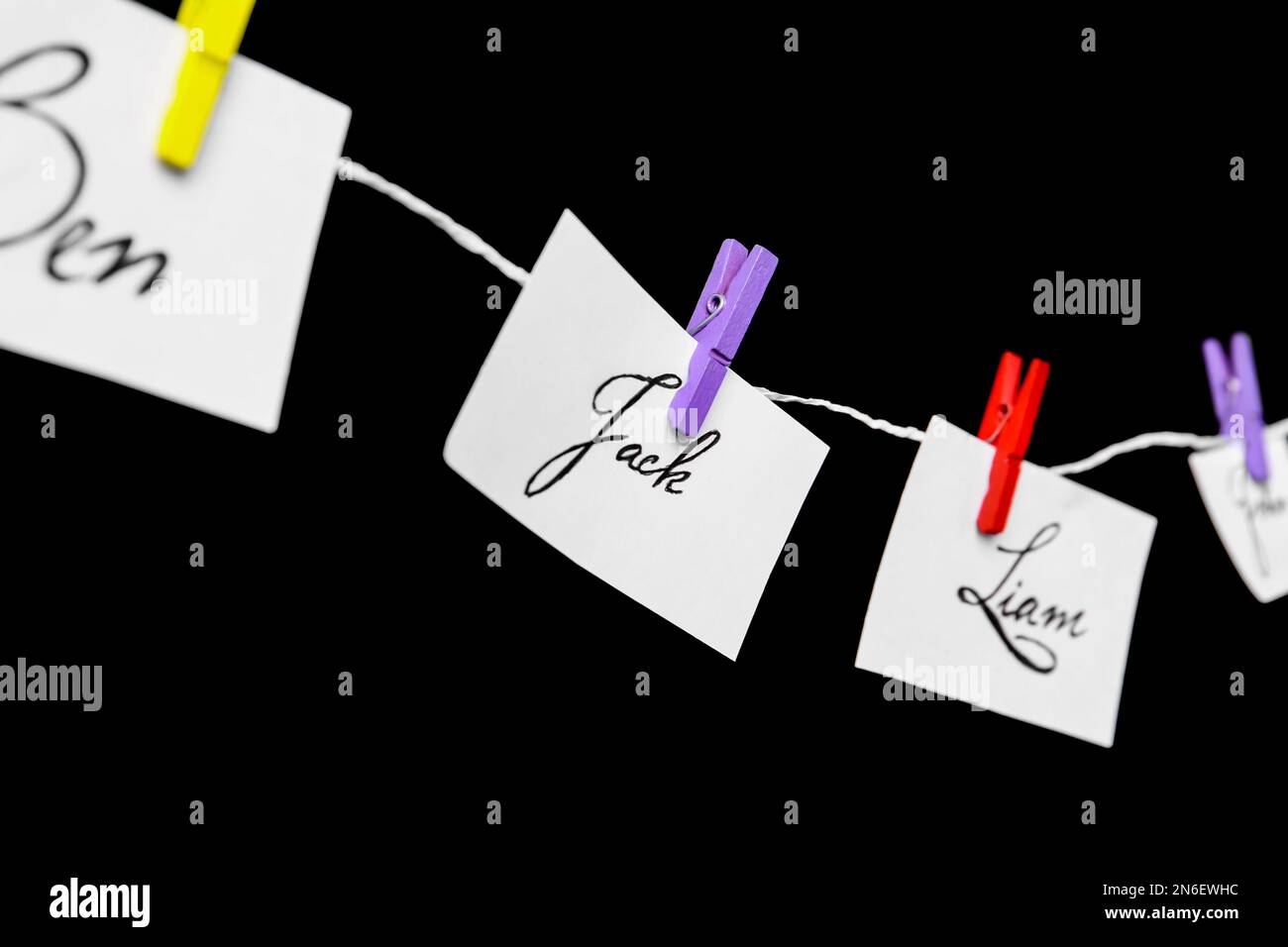 Paper pieces with baby names on rope against black background, closeup ...