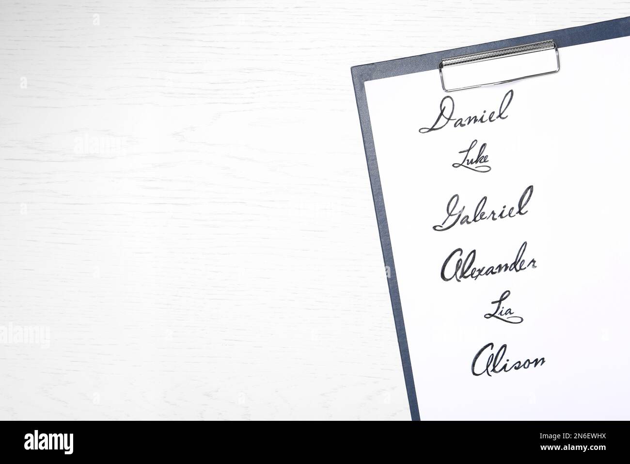 Clipboard with written different baby names on white wooden table, top ...