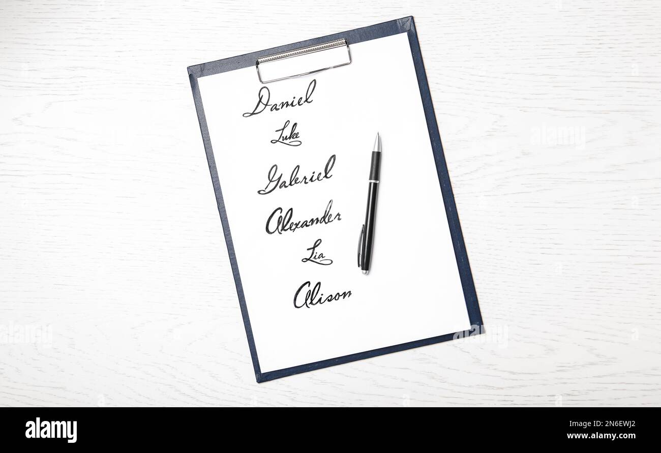 Clipboard with written different baby names and pen on white wooden ...