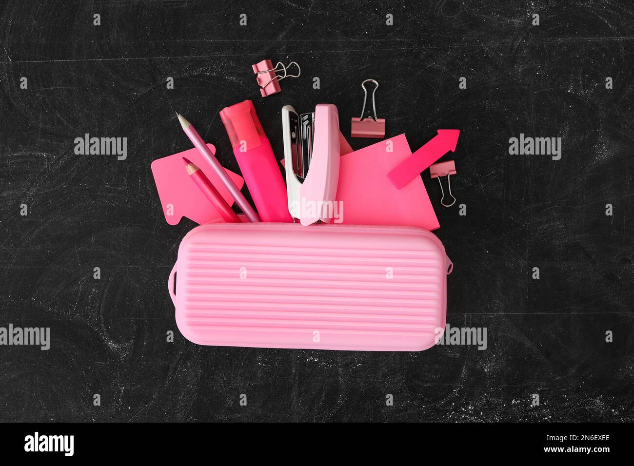 Pink pencil case and different stationery on blackboard, flat lay. Back ...
