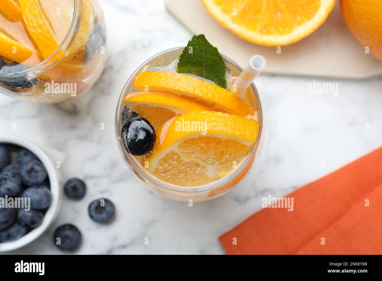 Flat lay composition of delicious orange lemonade with soda water, mint and blueberries on white ...