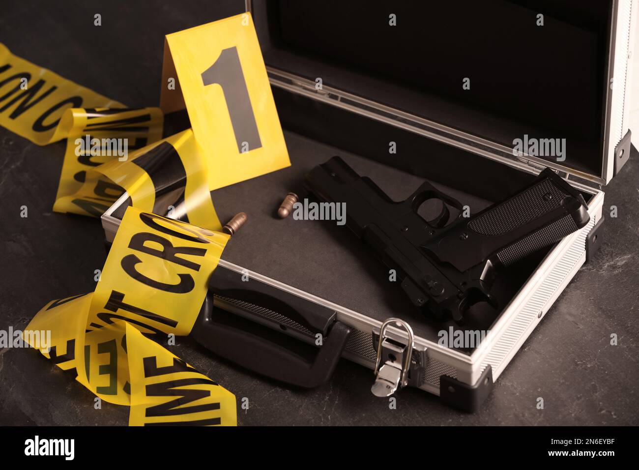 Open case with gun, bullets and crime scene marker on black table ...