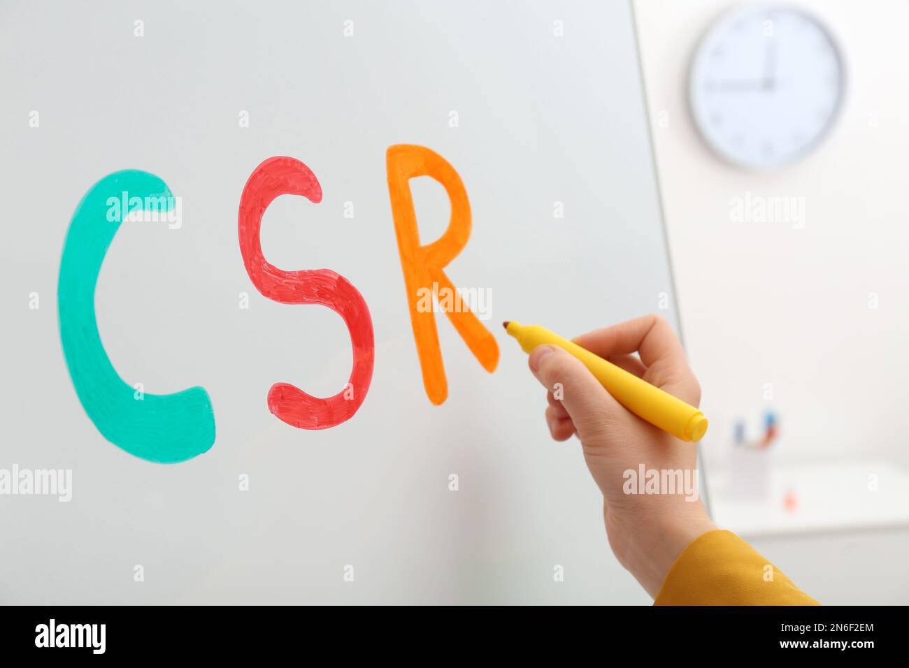 Woman writing abbreviation CSR on magnetic whiteboard, closeup ...