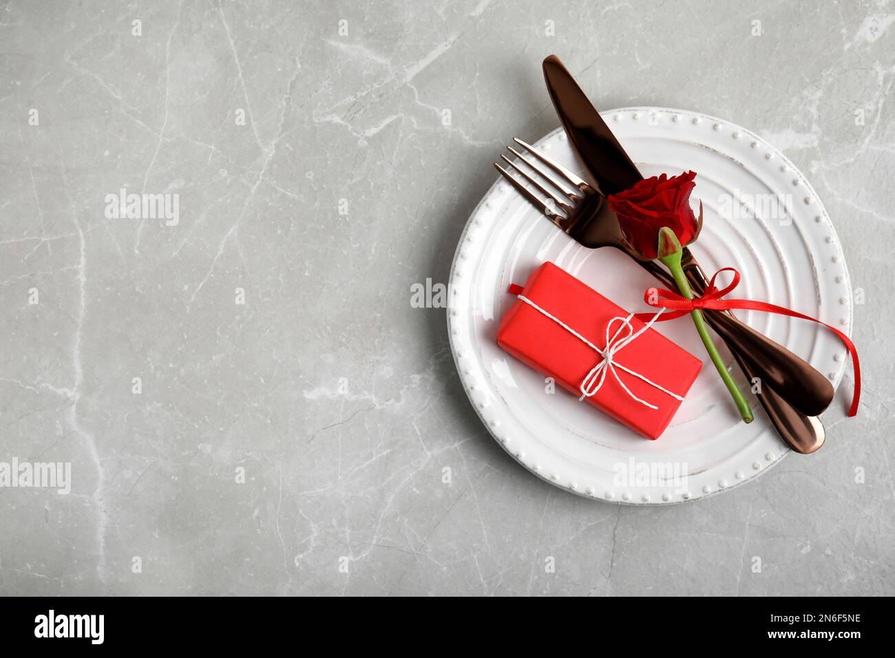 Beautiful place setting with gift box on light grey table, top view and space for text ...