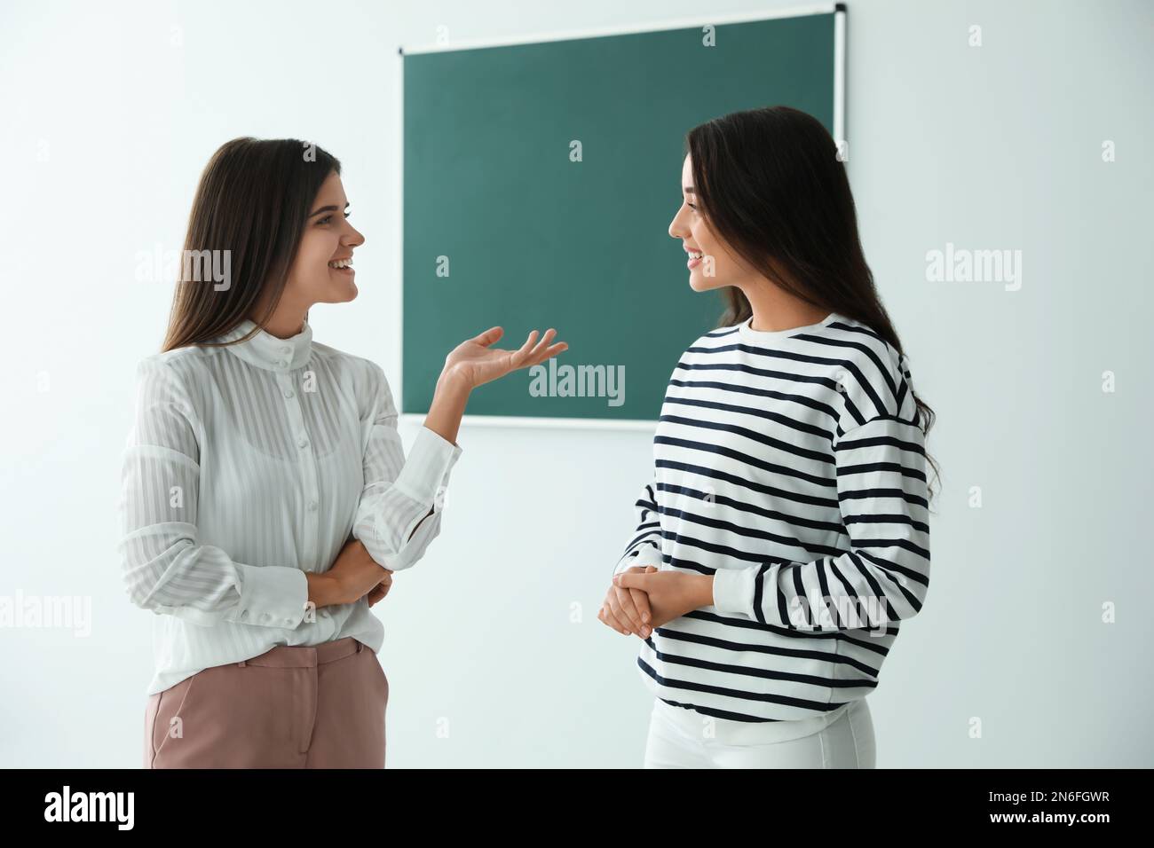 Young women talking near green chalkboard in classroom Stock Photo - Alamy
