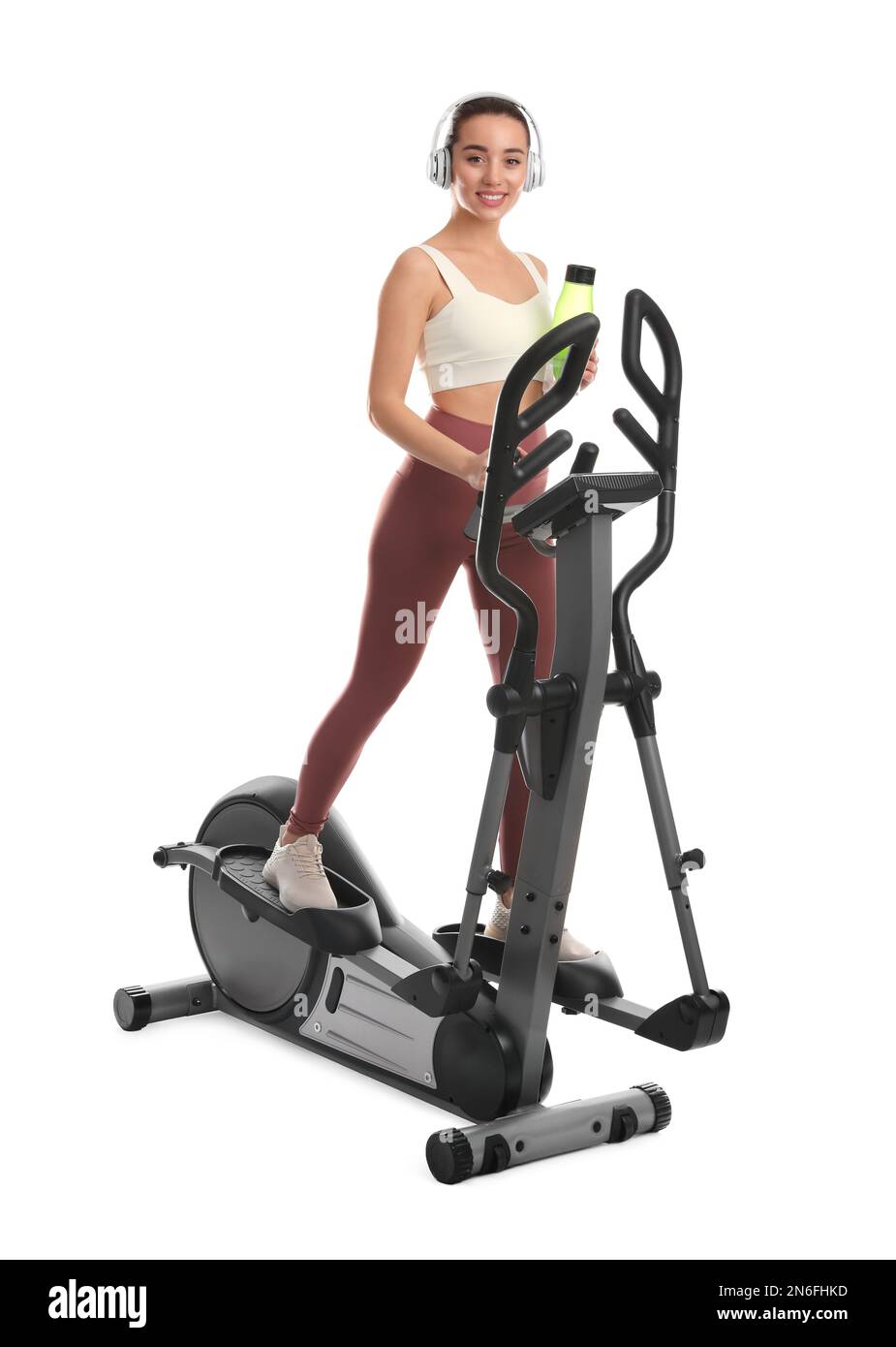 Woman with bottle using modern elliptical machine on white background ...