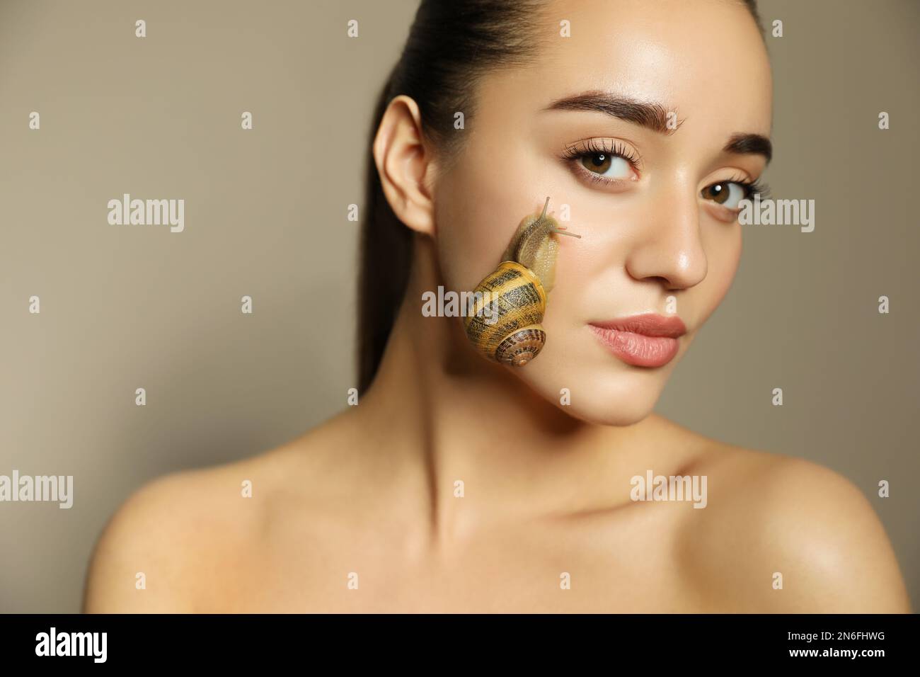 Beautiful young woman with snail on her face against beige background ...