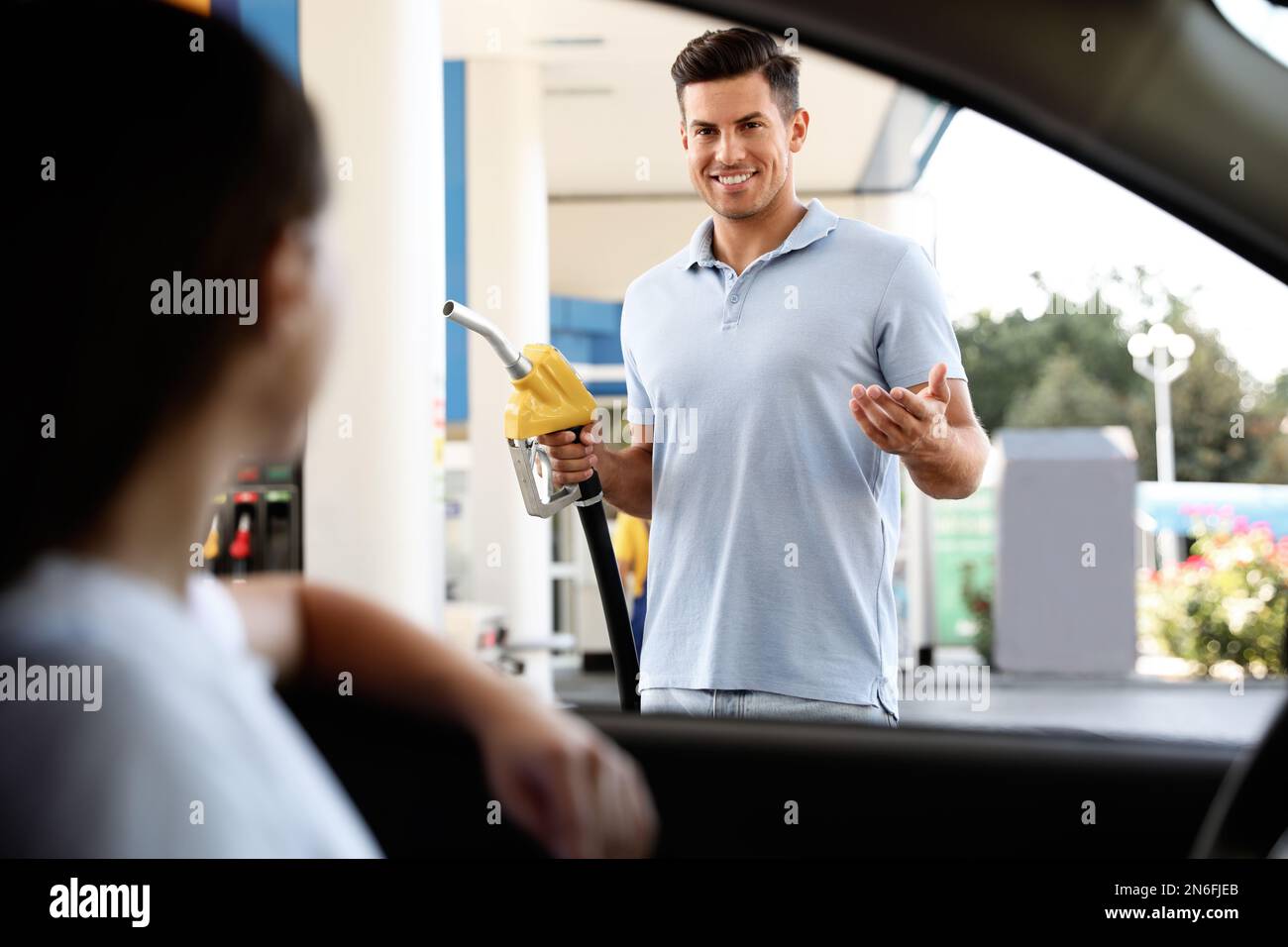 Man with fuel pump nozzle talking to his girlfriend at self service gas ...