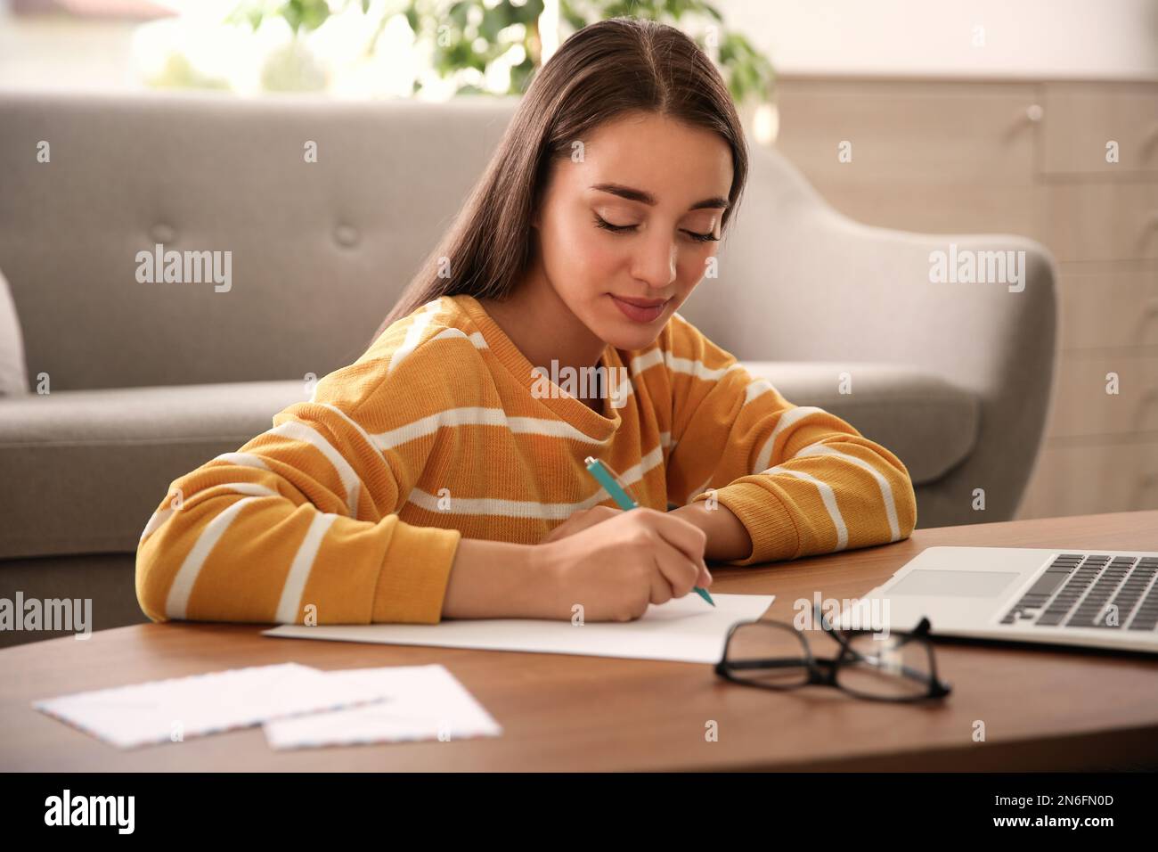 Woman writing letter at wooden table in room Stock Photo - Alamy