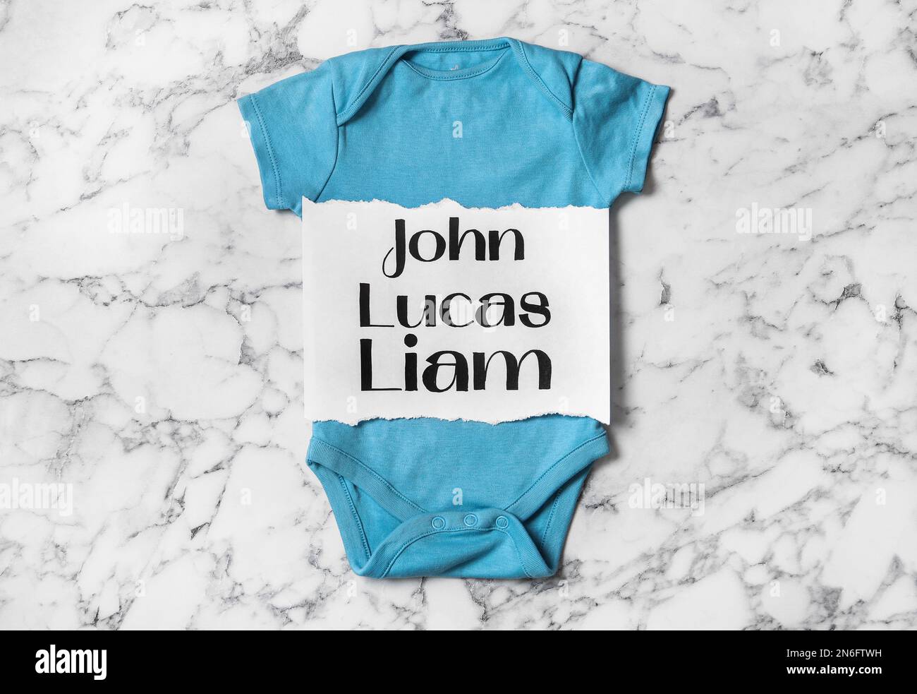 Bodysuit with different baby names on white marble background, top view ...