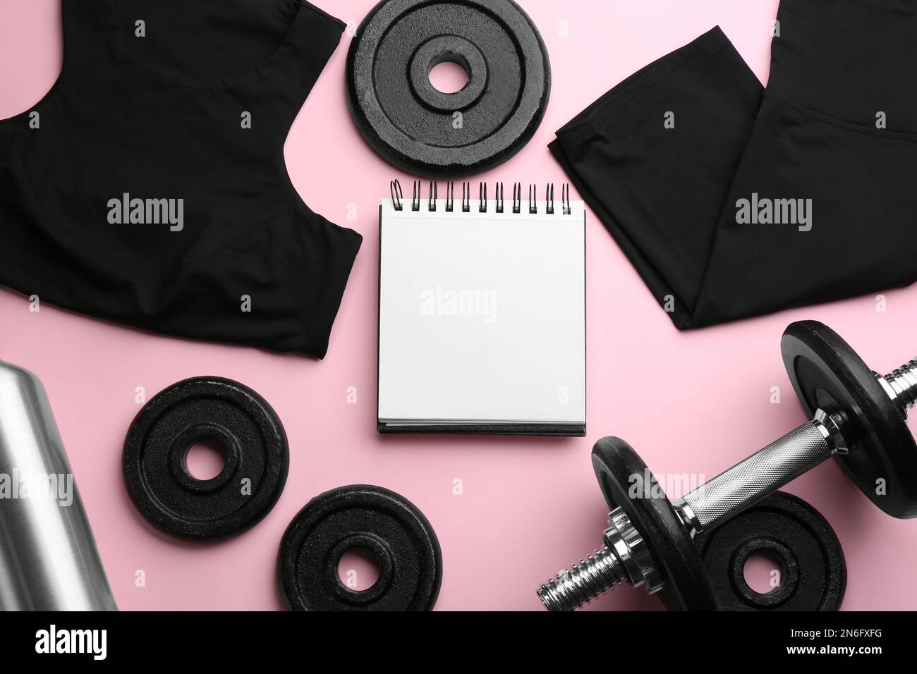 Flat lay composition with sportswear, notebook and dumbbell on pink ...