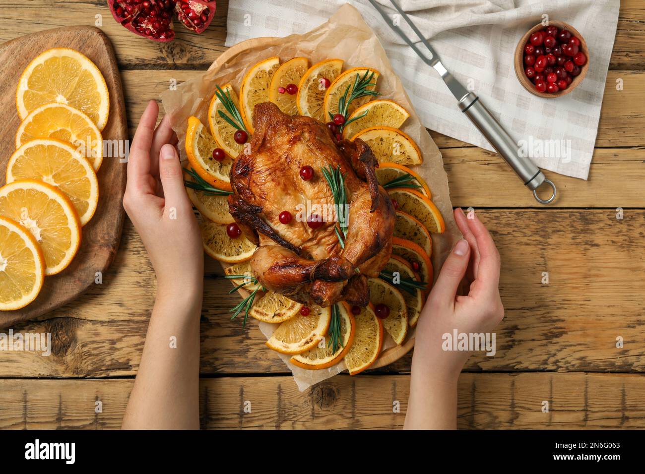 Woman holding baked chicken with orange slices at wooden table, closeup ...
