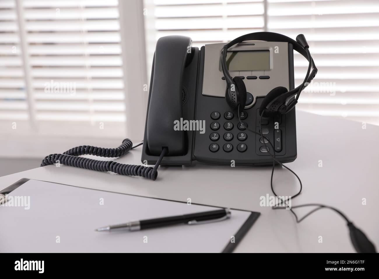 Desktop telephone with headset on white table in office. Hotline ...
