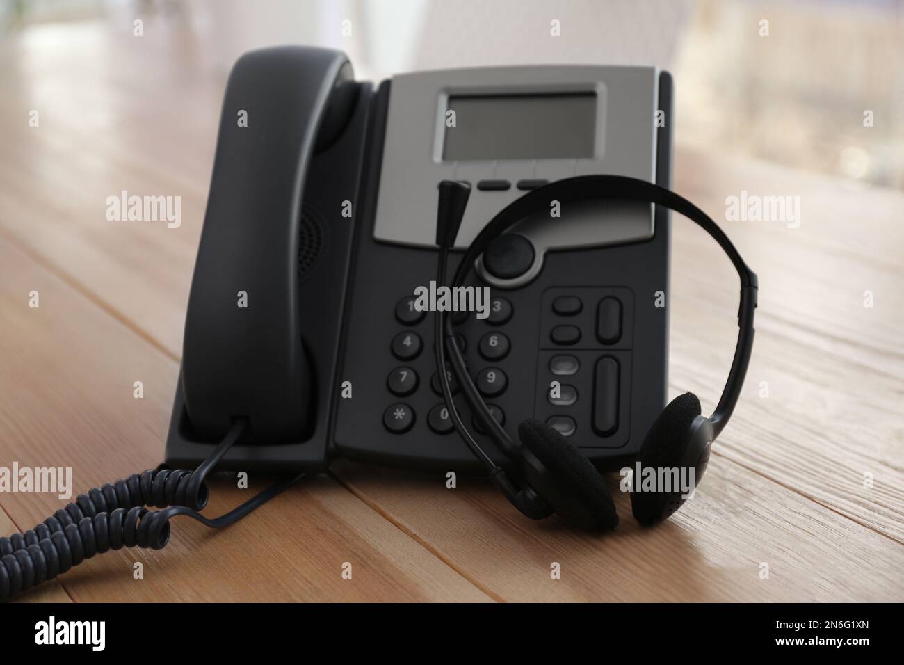 Office desktop telephone and headset on wooden table. Hotline service ...