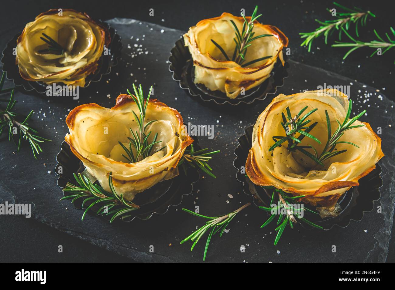 Baked crispy potato roses with rosemary in black tartlet forms on a ...