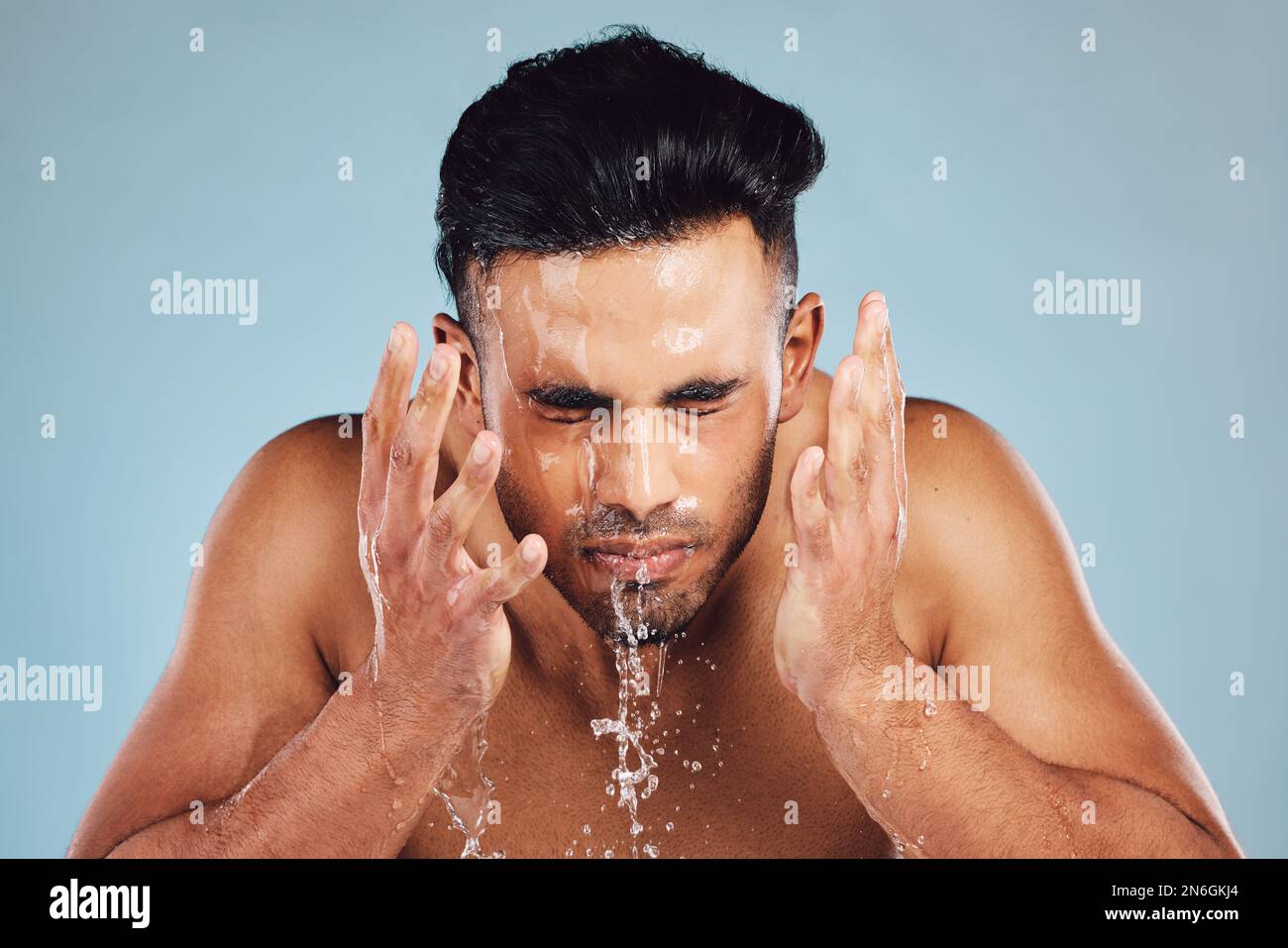 Man, water and hands in face wash for skincare, fresh clean hygiene or grooming against studio ...