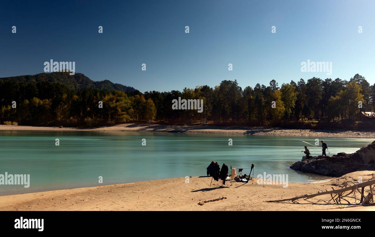 Fishing tackle stands on the sandy bank of the Katun River against the ...