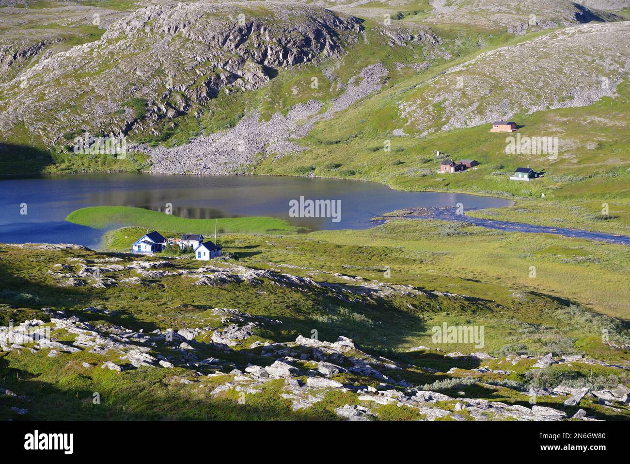 Green land with barren, stony mountains and a lake, single cabins ...
